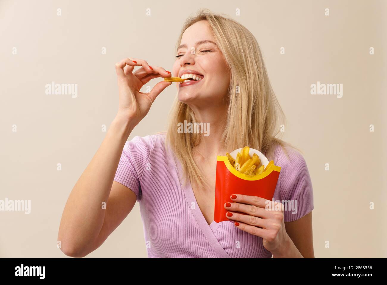 Cheerful beautiful girl laughing while eating french fries isolated ...