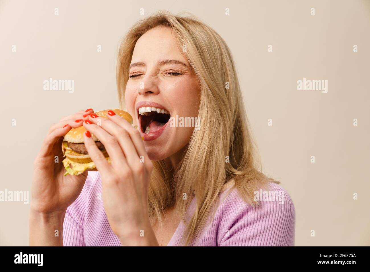 Happy beautiful hungry girl eating hamburger on camera isolated over ...