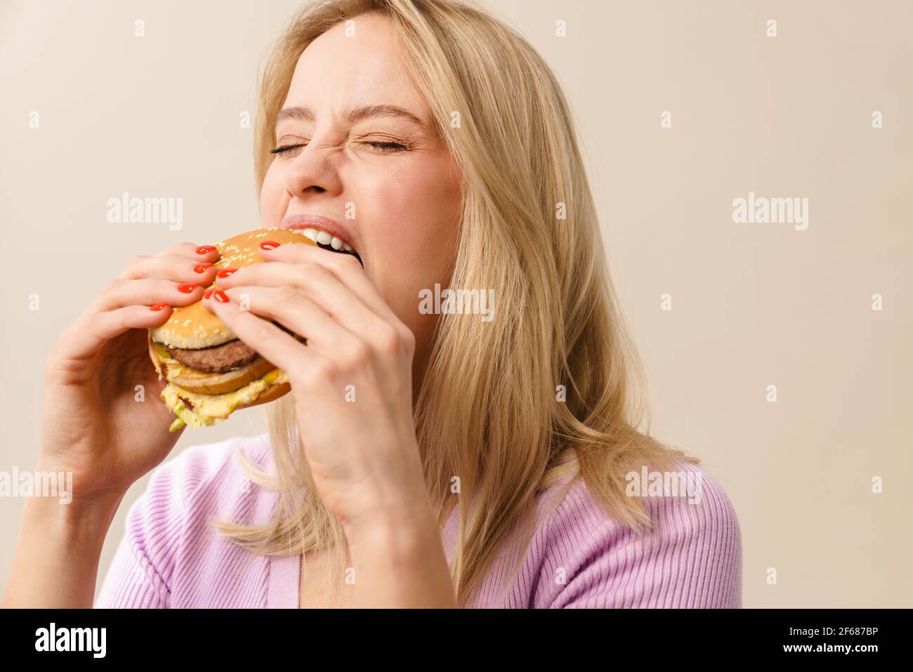 Happy beautiful hungry girl eating hamburger on camera isolated over ...
