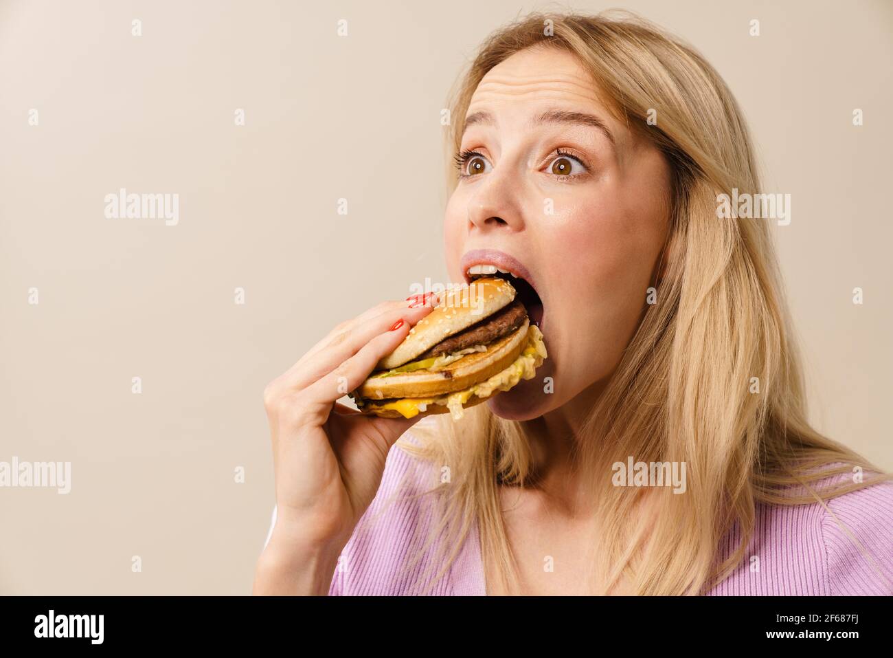 Surprised beautiful hungry girl eating hamburger on camera isolated ...