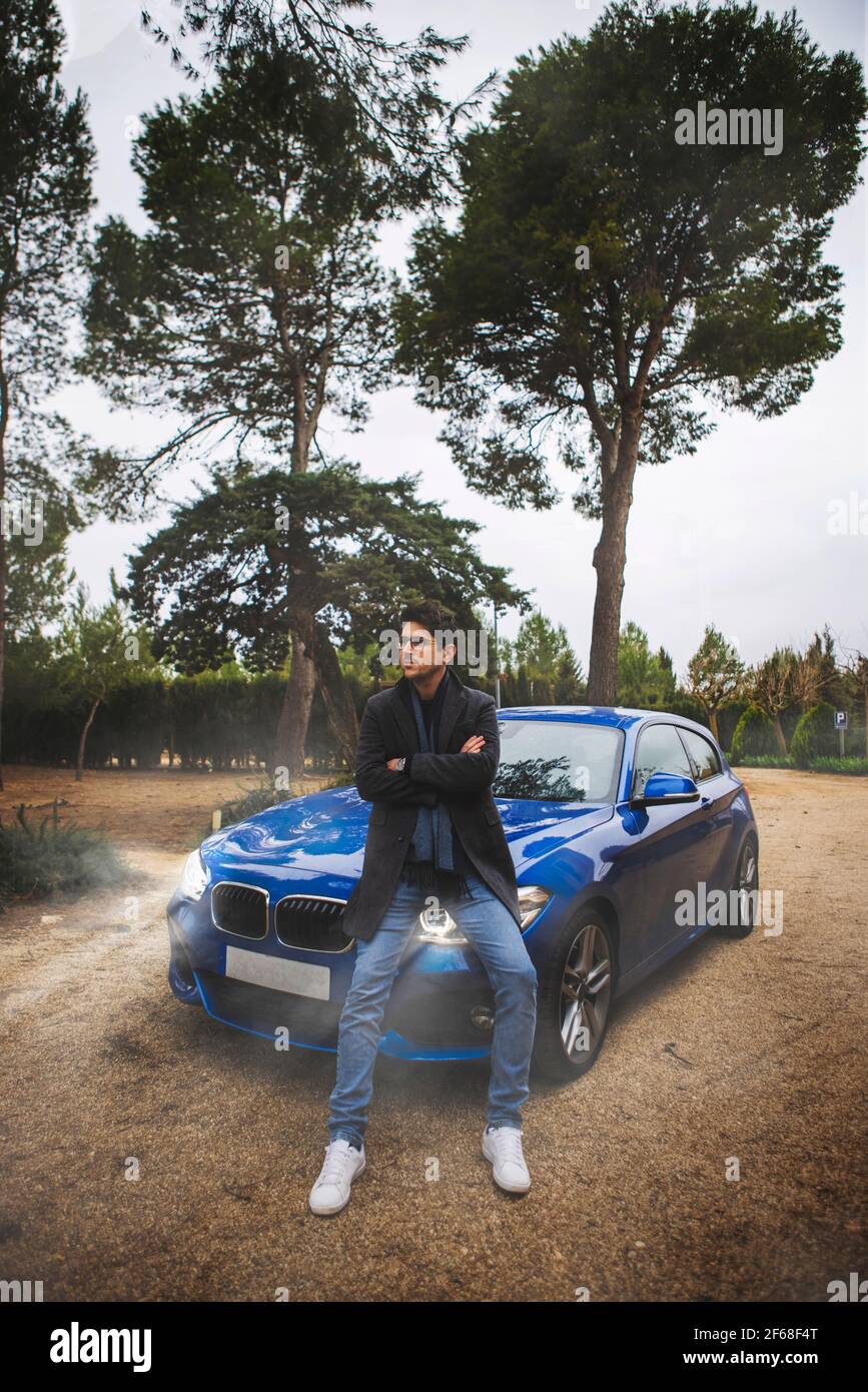 Young man sitting in front of his blue car while waiting Stock Photo ...