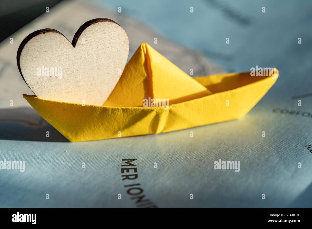isolated origami yellow boat with wooden heart on world map. travel ...