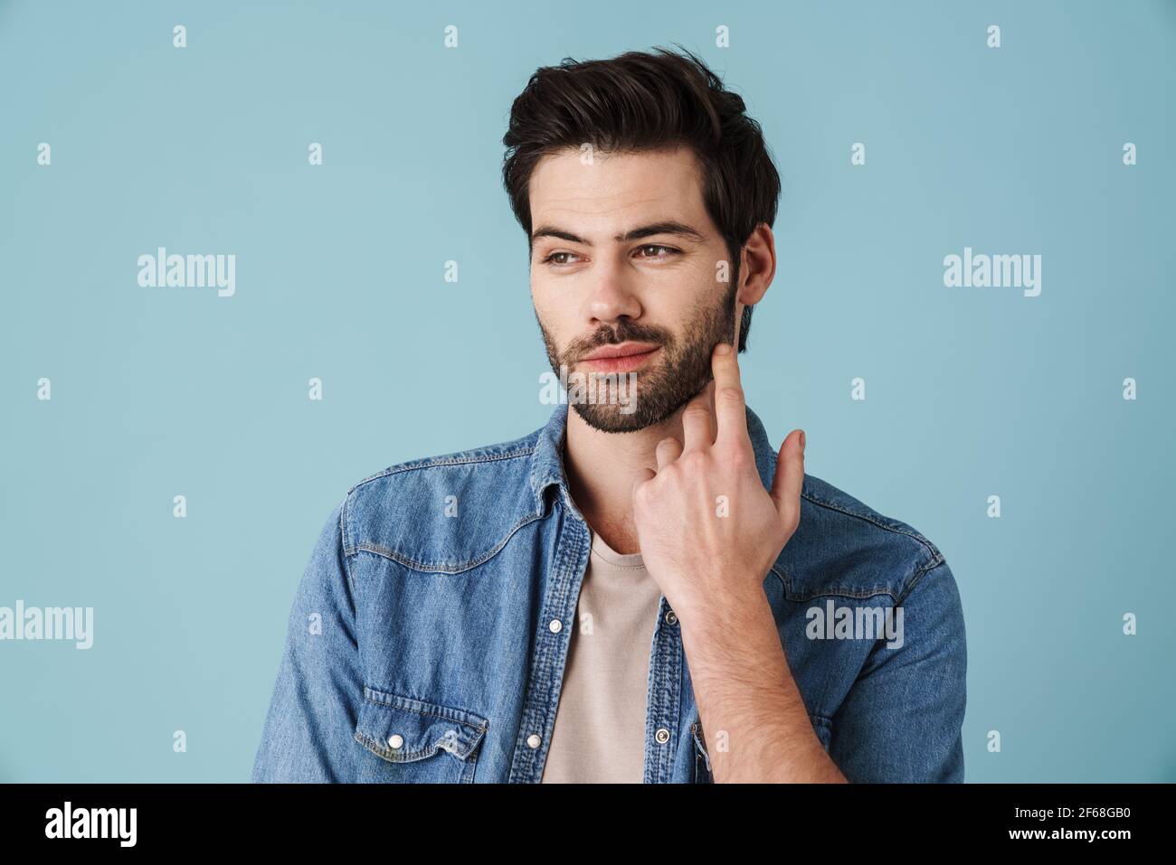 Young handsome unshaven man posing at camera isolated over blue ...
