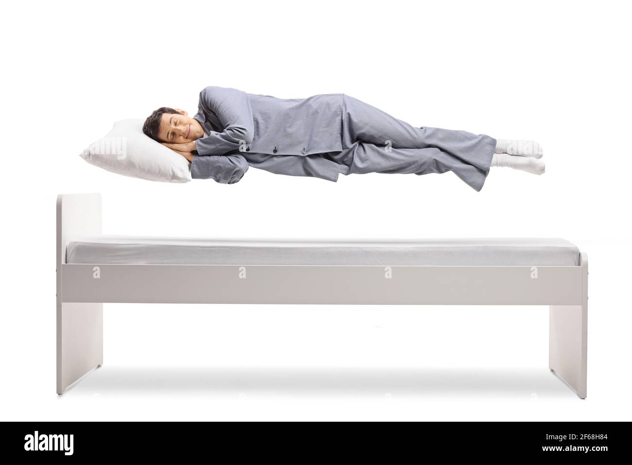 Man in pajamas sleeping and floating above a bed isolated on white ...