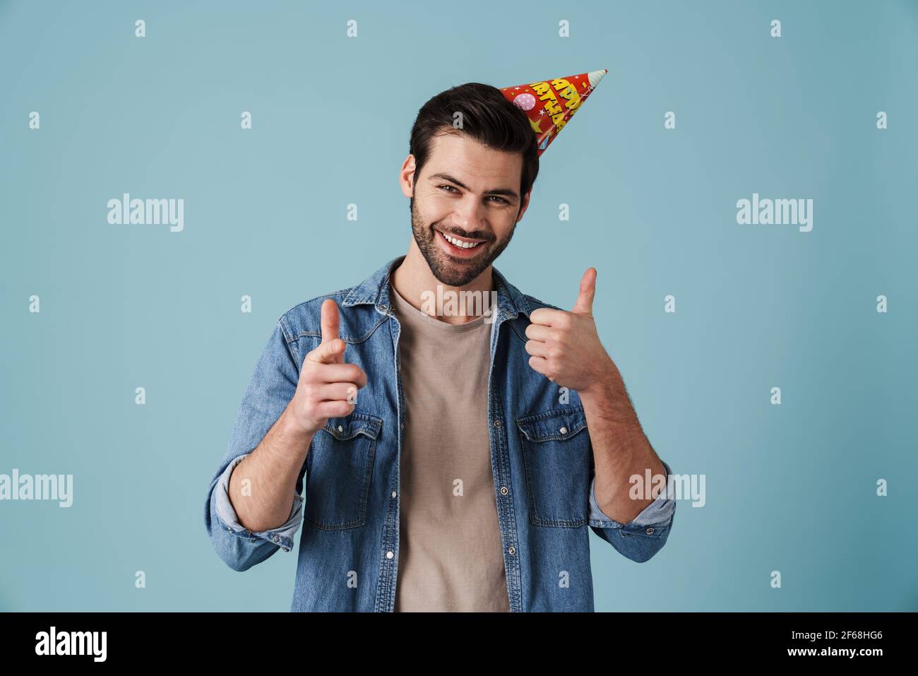 Young handsome excited man in party cone showing thumbs up isolated ...