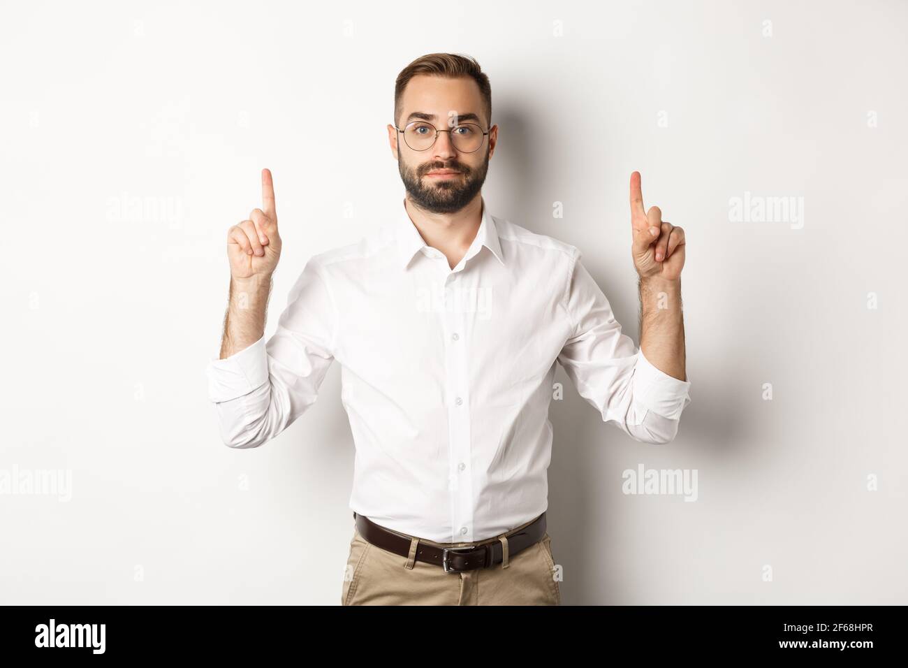 Young bearded businessman pointing fingers up, showing promo offer, standing over white ...