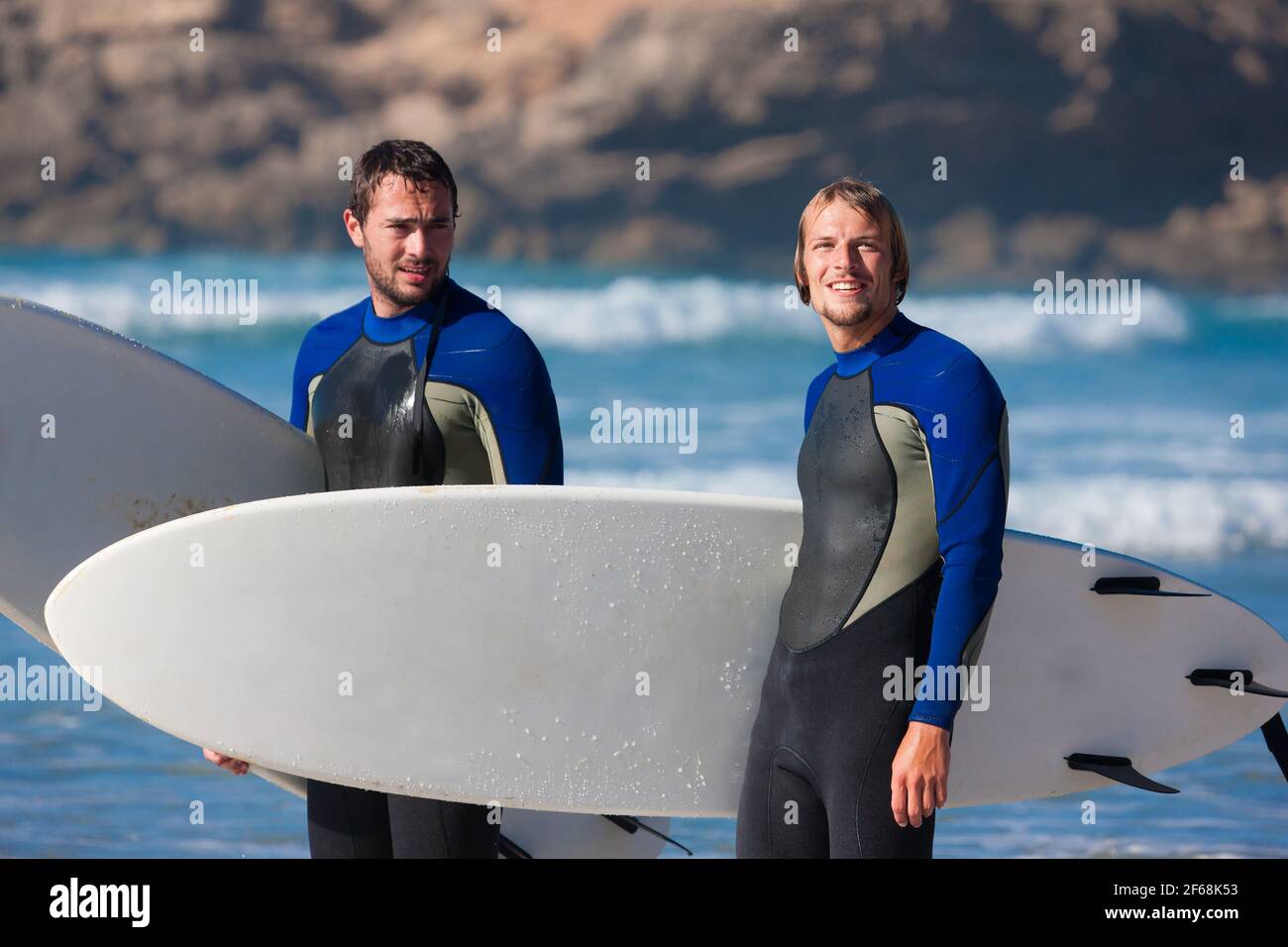 Two surfers with their surf boards standing on the beach discussing the ...