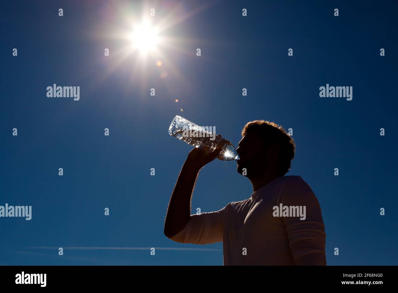 Sportive man drinking water from a bottle against a blue sky background ...