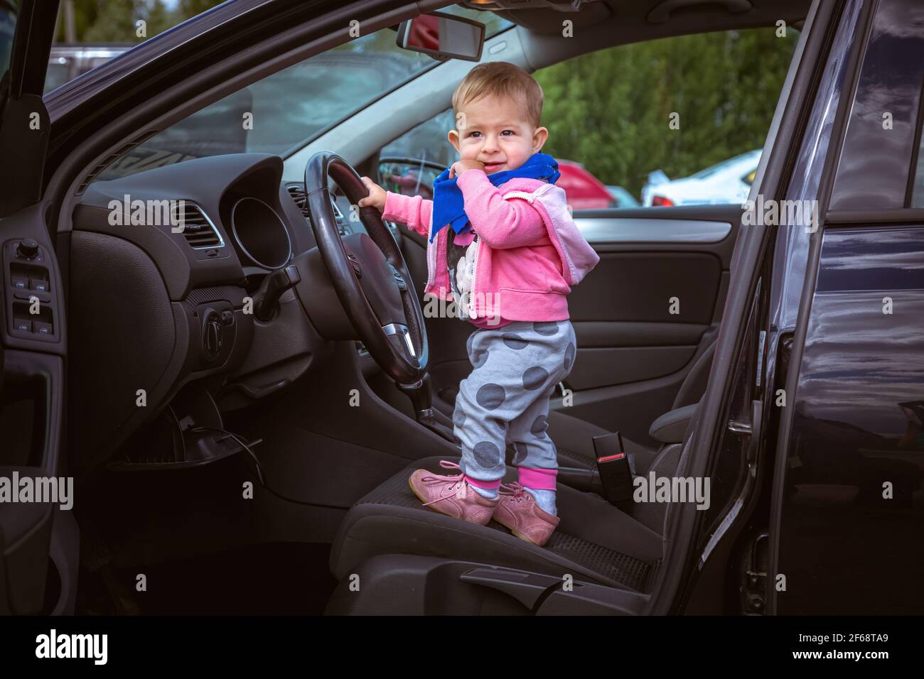 Little kid in a car. Stands in the driver's seat and holds the wheel ...