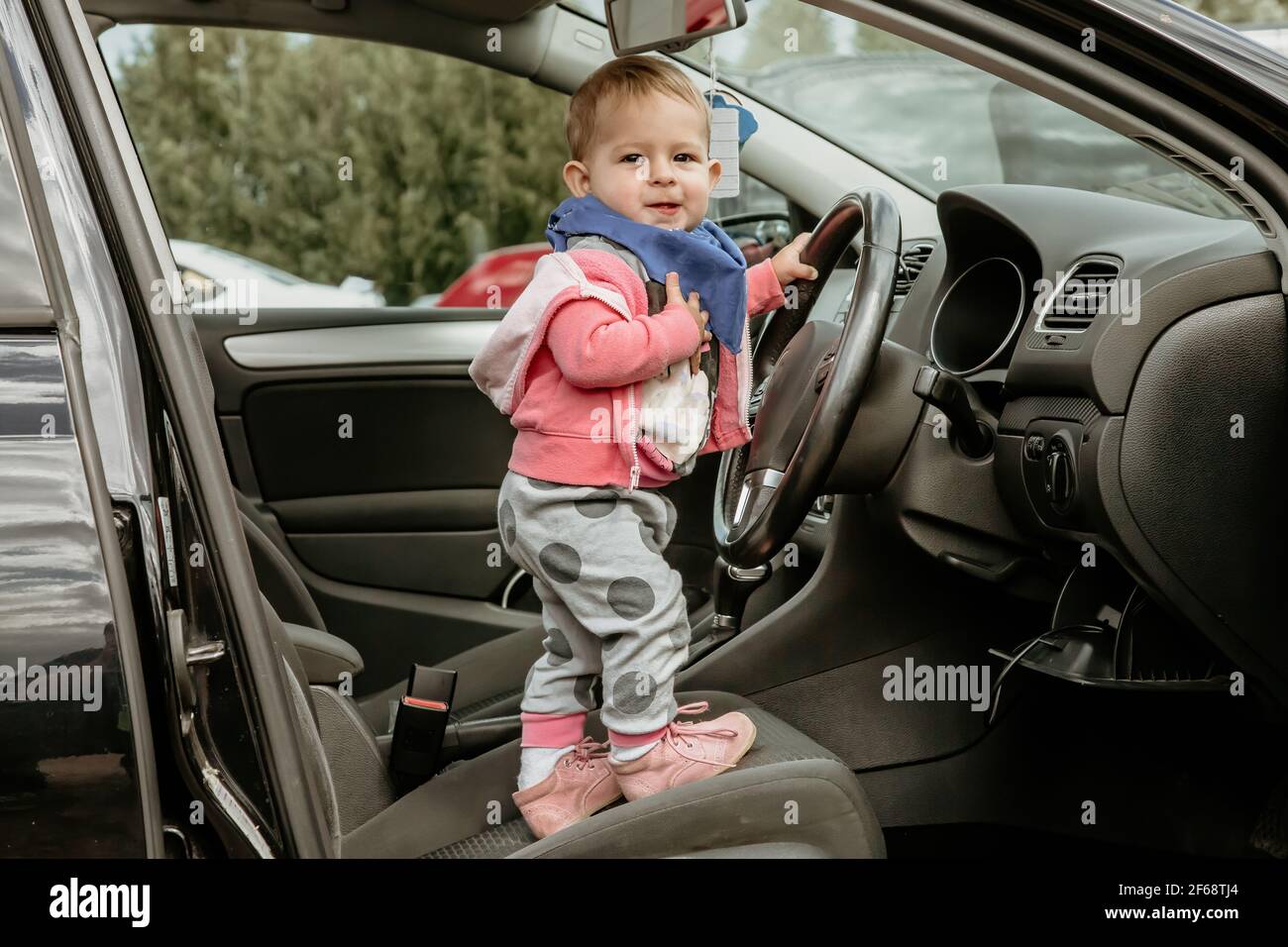 Little kid in a car. Stands in the driver's seat and holds the wheel ...