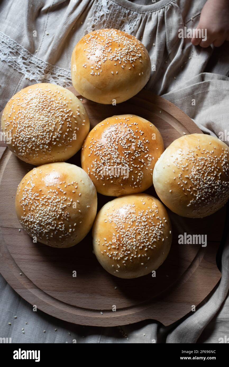 hamburger buns with sesame seeds on a linen sundress and a wood board ...