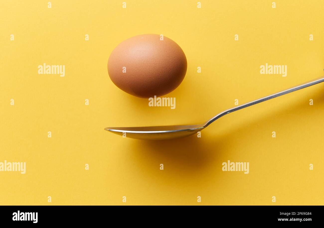 single brown chicken egg falling into spoon on yellow background Stock ...