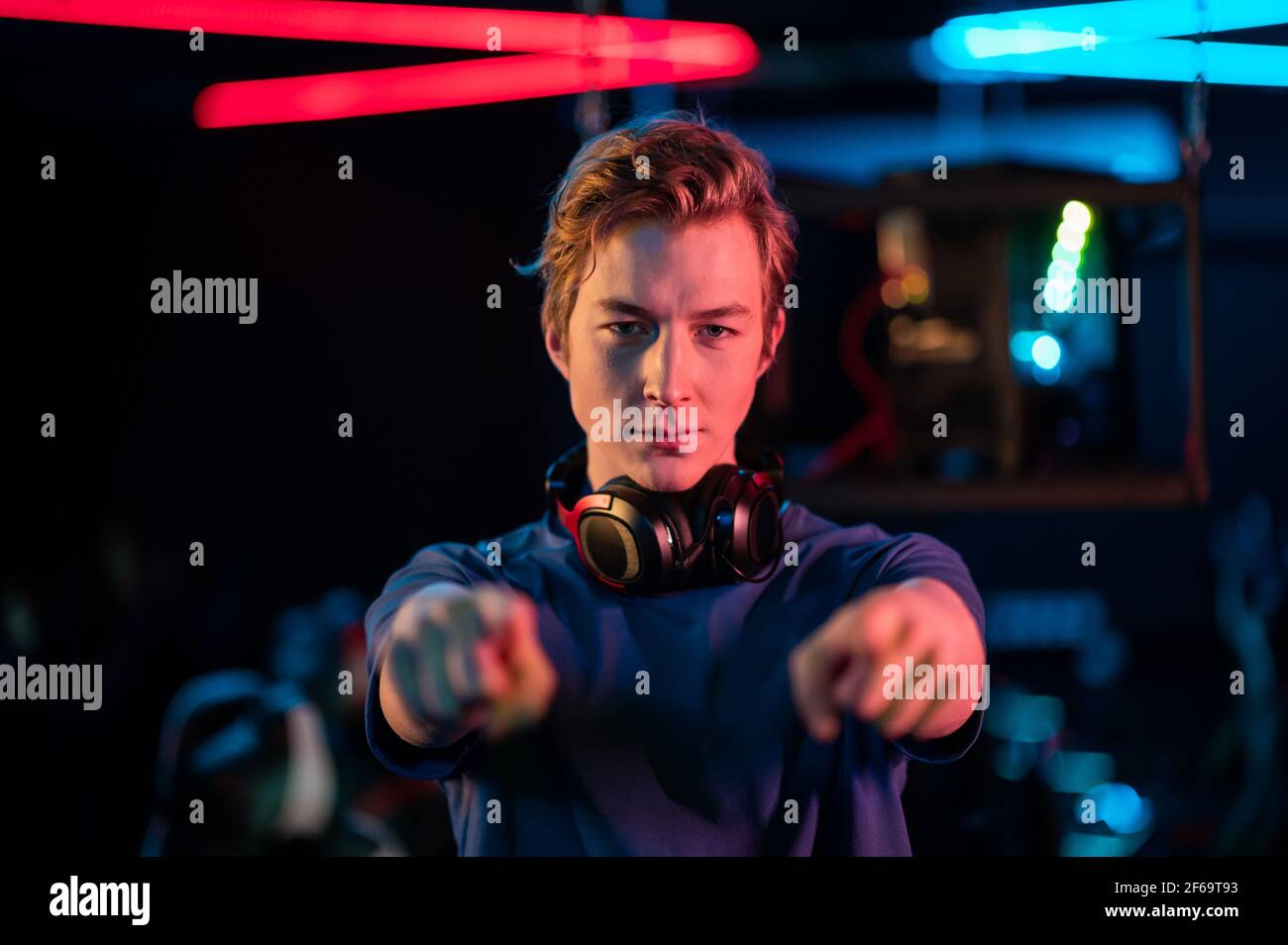 A cool gamer in a headset around his neck shows his hands to the camera ...