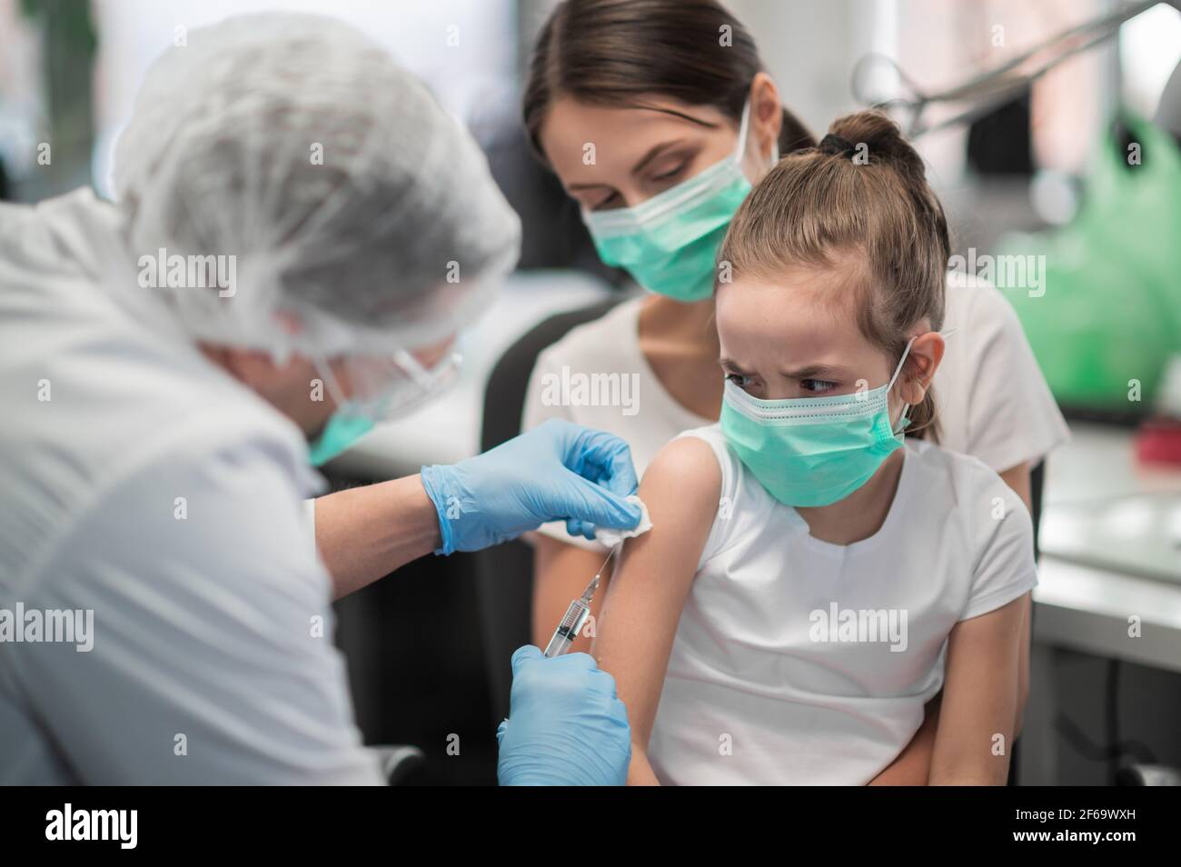 A doctor gives a frightened girl an injection in the shoulder to ...