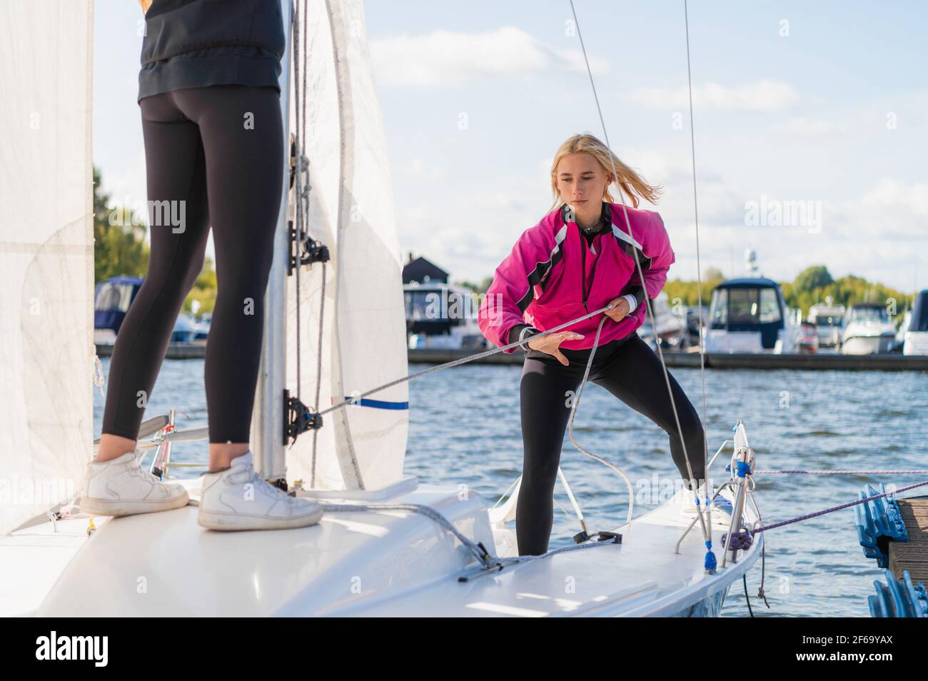 On the pier, two pretty girls pull sails on a boat to participate in a ...