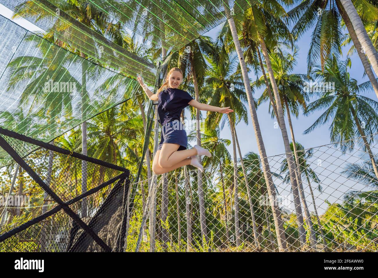 Young woman jumping on an outdoor trampoline, against the backdrop of ...
