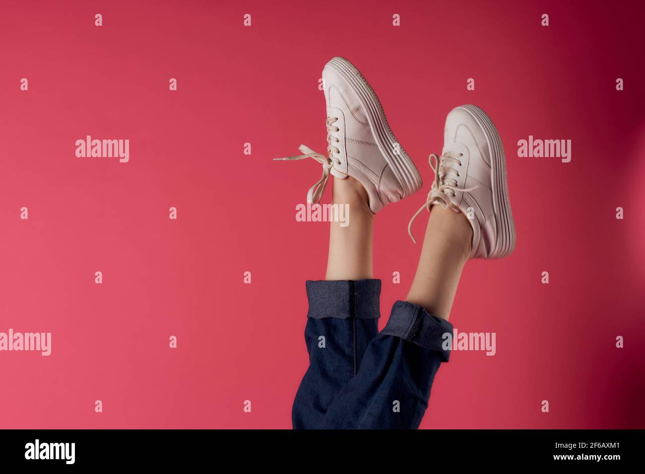 inverted female legs in white sneakers fashion studio pink background ...