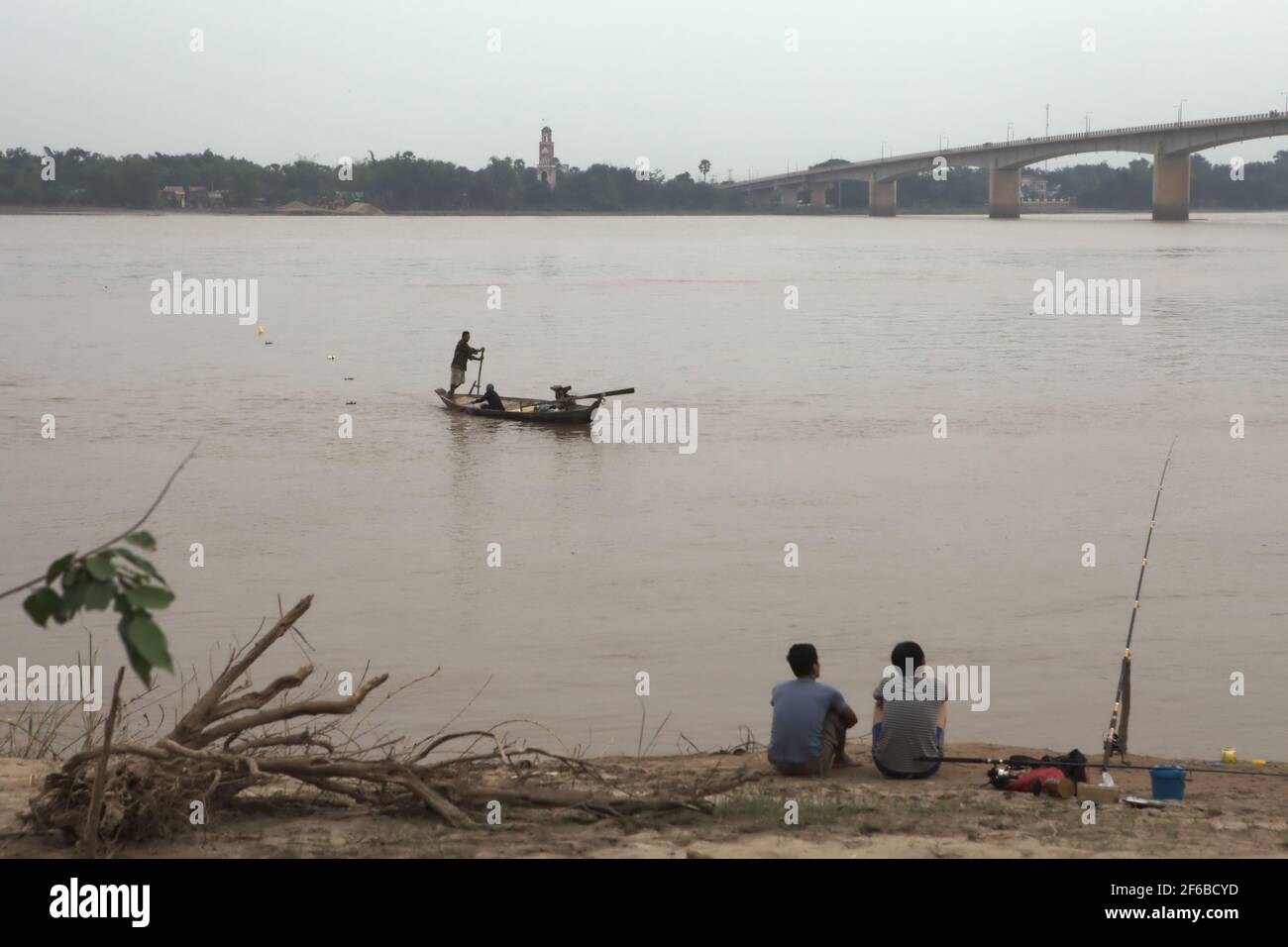 Young men fishing from riverbank as a fishing boat passes, floating on ...