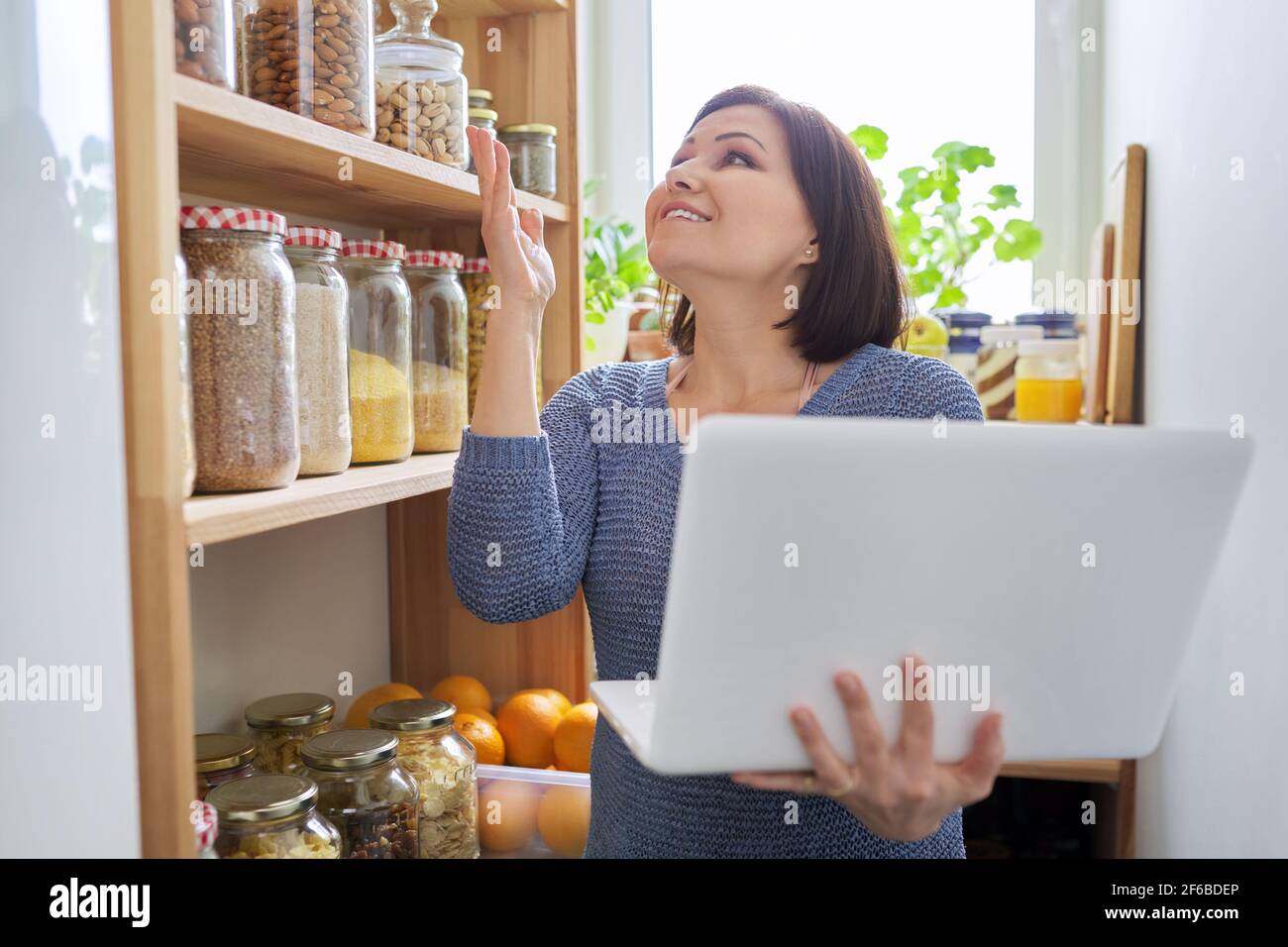 Woman in kitchen pantry with stored products, holding laptop Stock ...