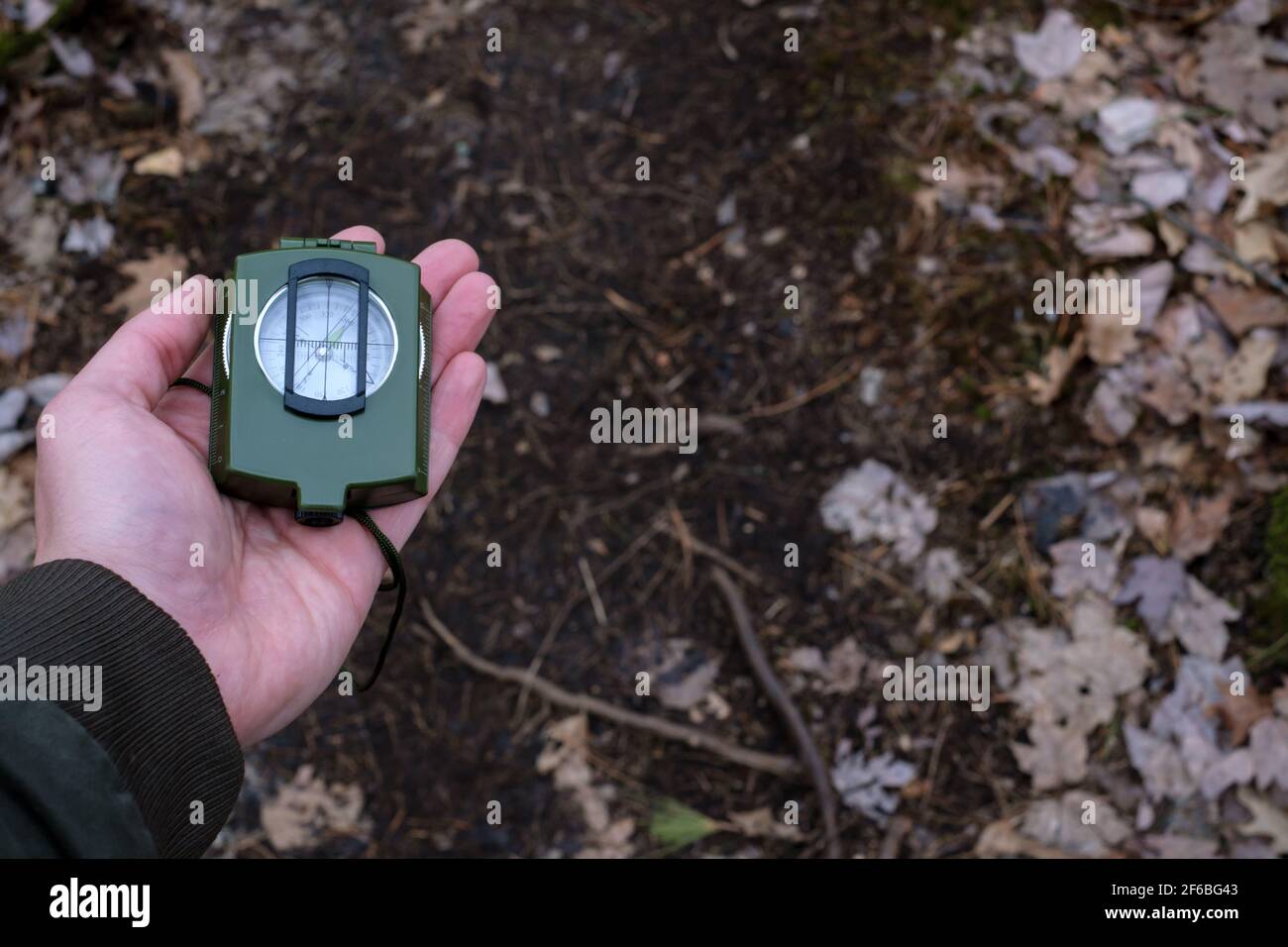 A hand holds a green tactical prismatic compass over a forest trail ...