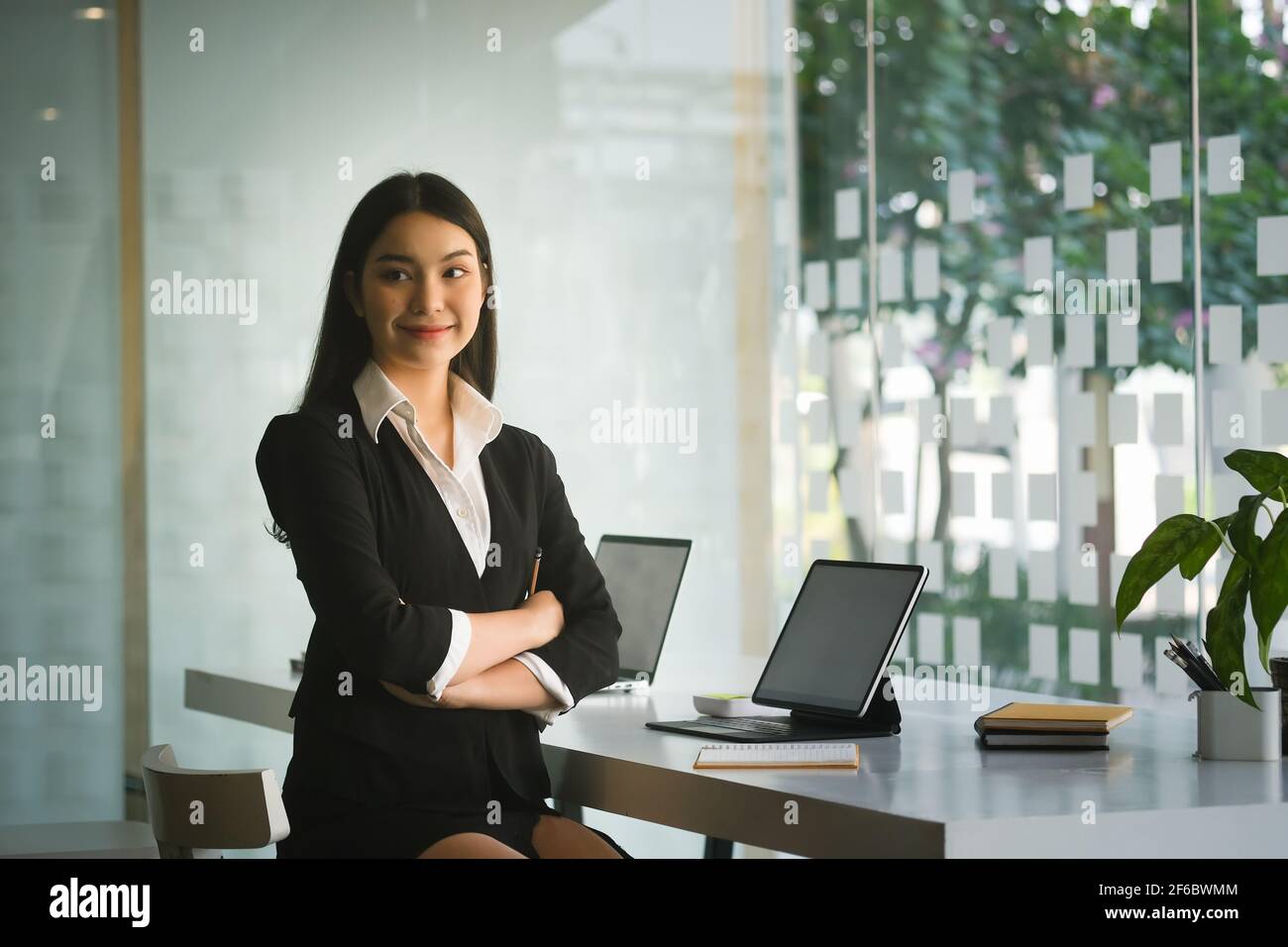 Confident businesswoman in suit sitting with arms crossed and smiling ...