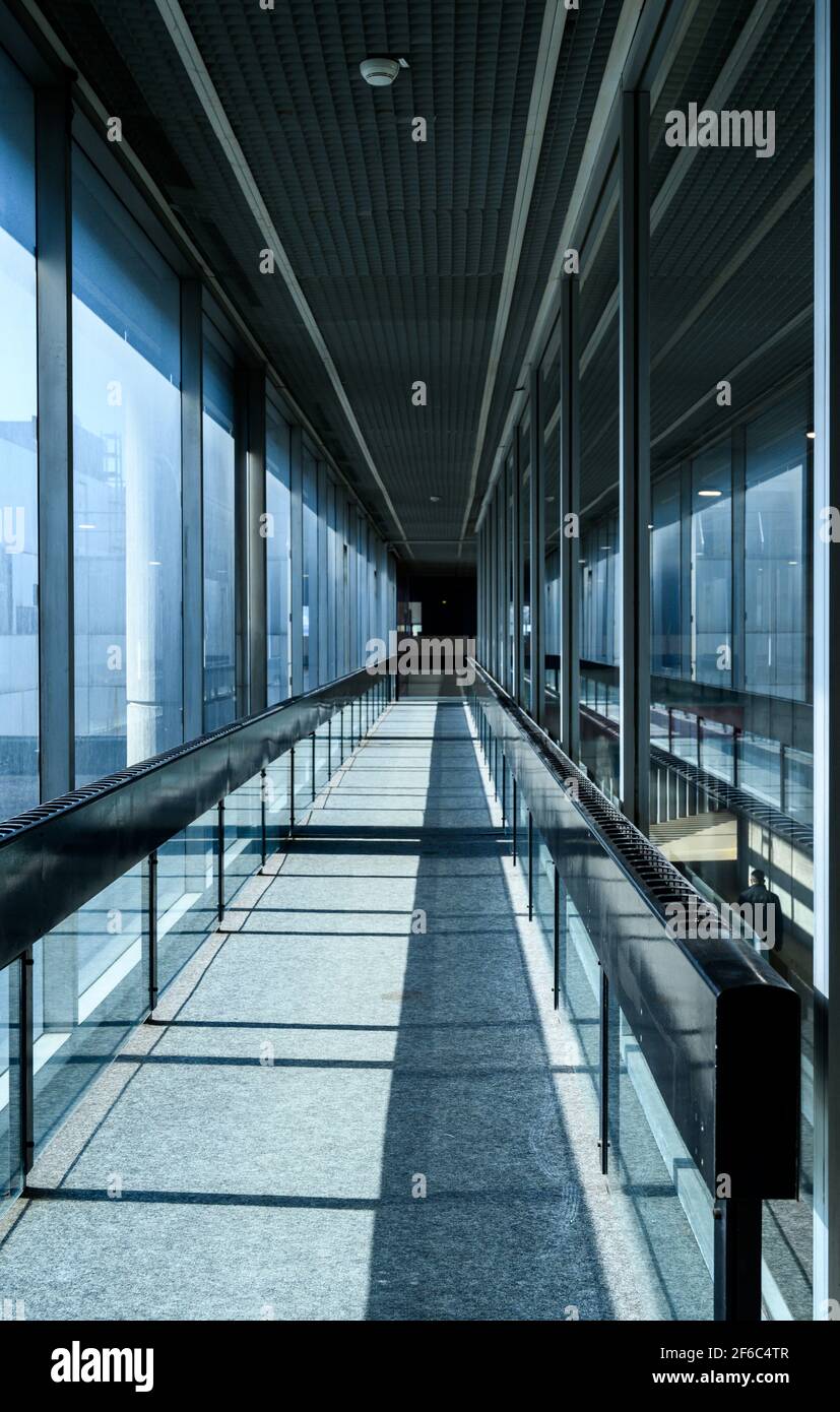 Long narrow corridor leading on outside of high building. Glass wall ...