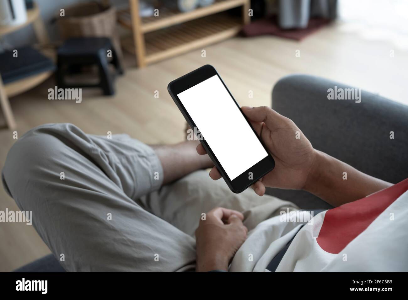 Casual man sitting on sofa and holding mobile phone wit white screen ...