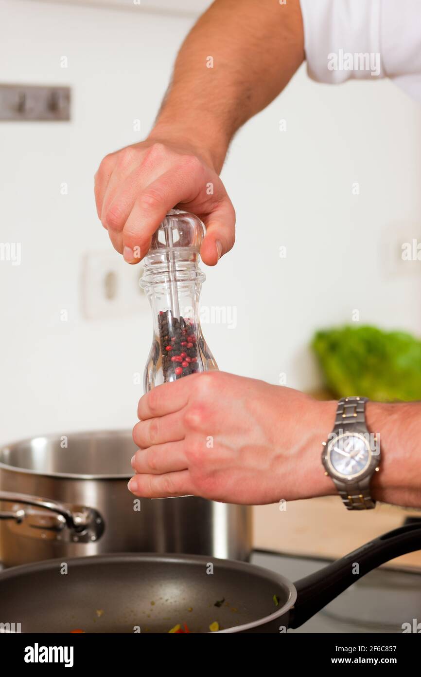 Man in the kitchen - only hands to be seen - is adding spices to food ...