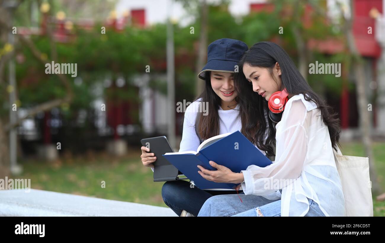 Two happy students reading book and talking each other in campus Stock ...
