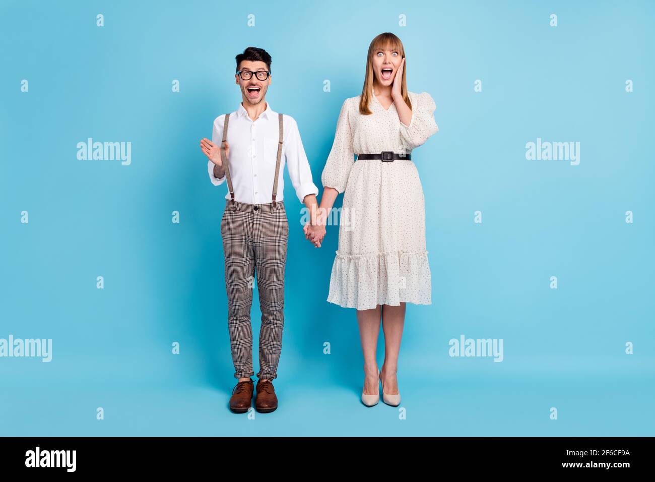 Photo of sweet impressed couple wear white outfit holding arms together ...
