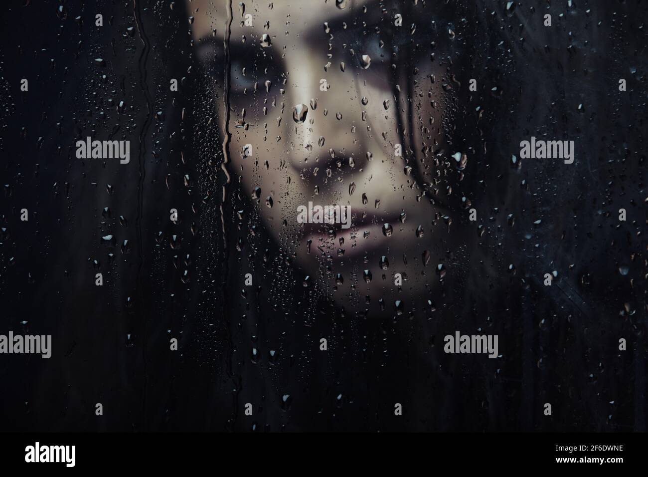 Sad woman at night behind the glass with rain drops Stock Photo - Alamy
