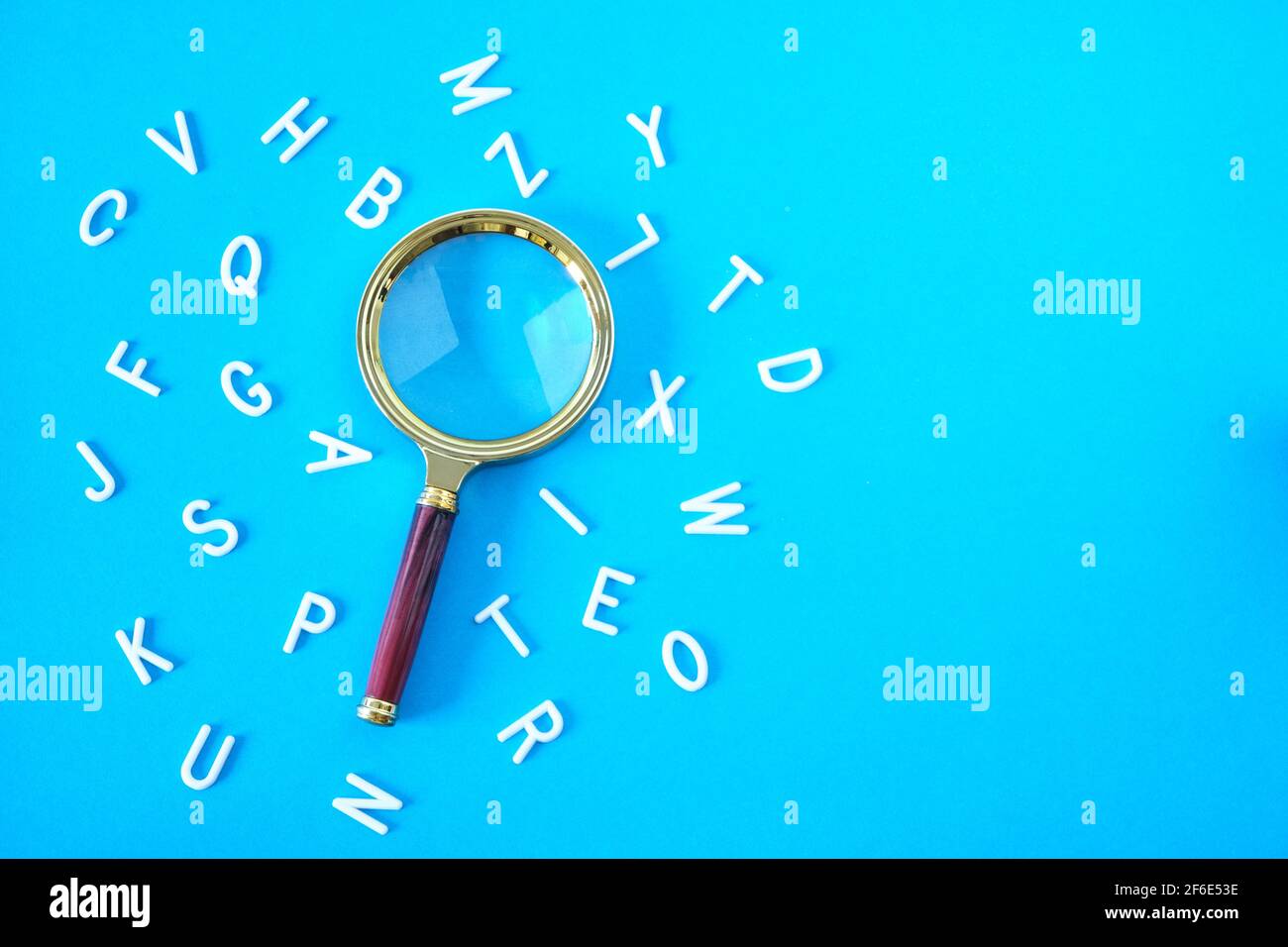 Magnifying glass on a blue background with scattered letters of the ...