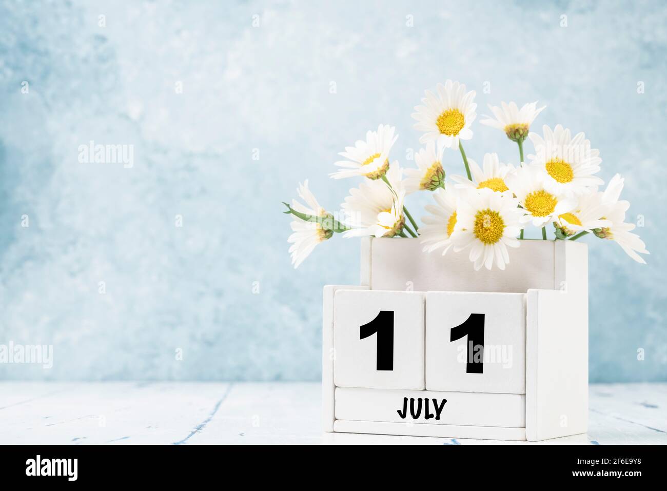 White cube calendar for July decorated with daisy flowers over blue ...