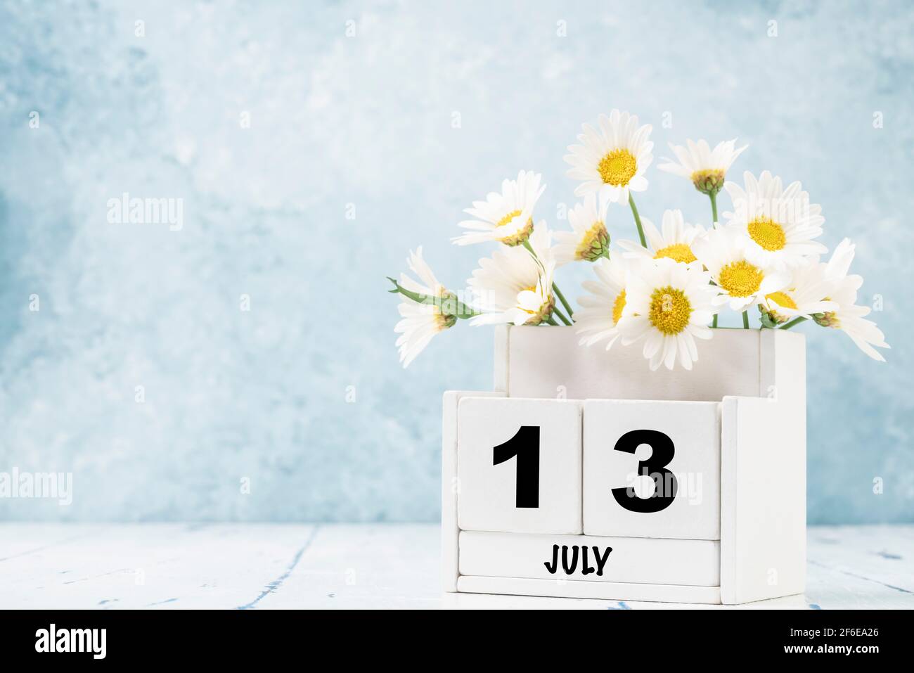 White cube calendar for July decorated with daisy flowers over blue ...