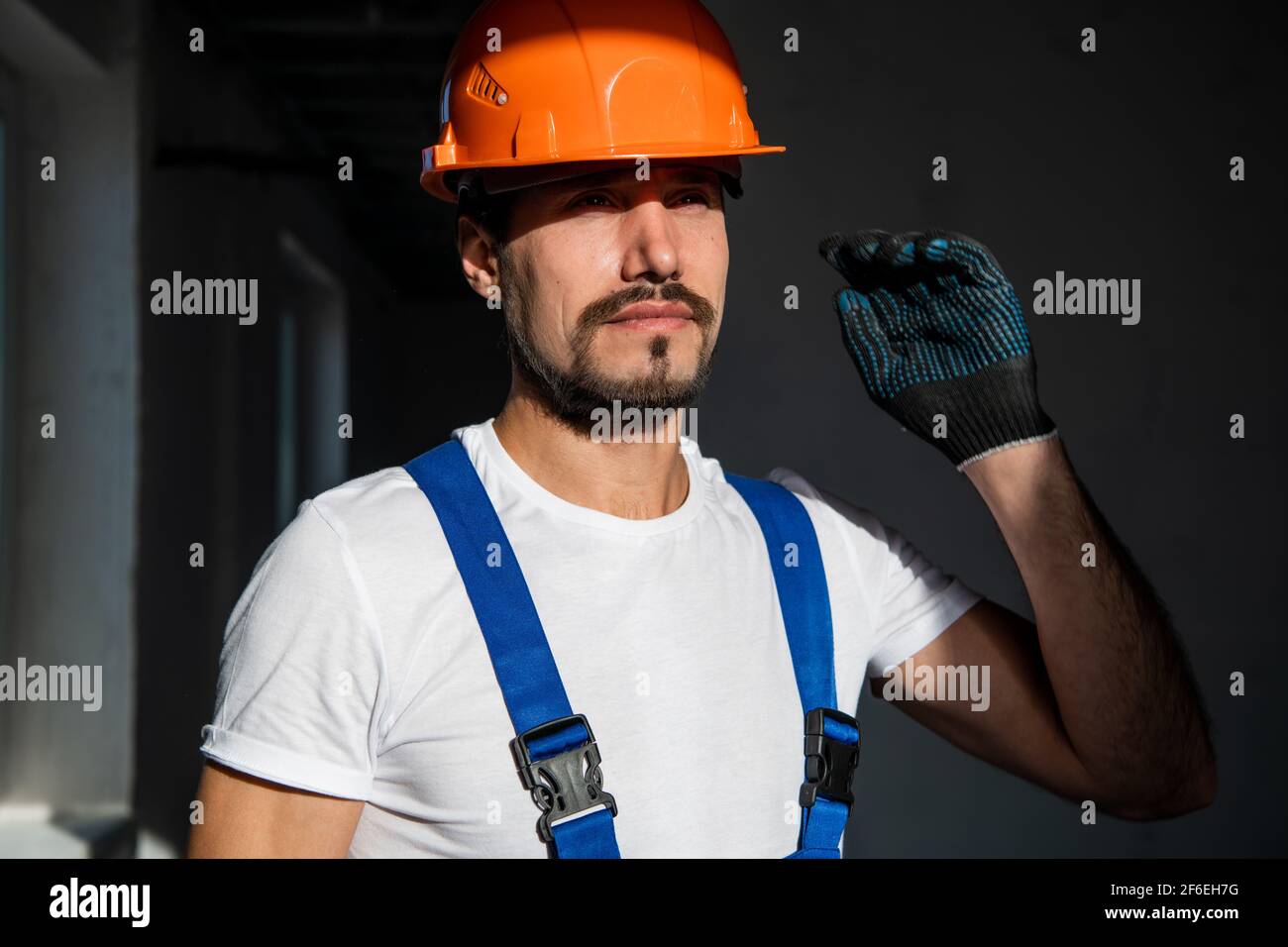 A builder in black gloves and a blue uniform puts a construction helmet ...