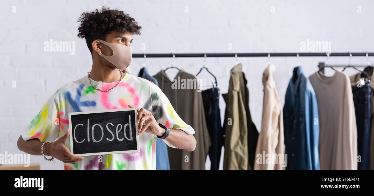 Young african american owner of showroom holding chalkboard with closed ...