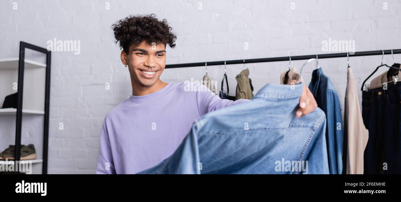 Smiling african american showroom owner holding denim shirt on blurred ...