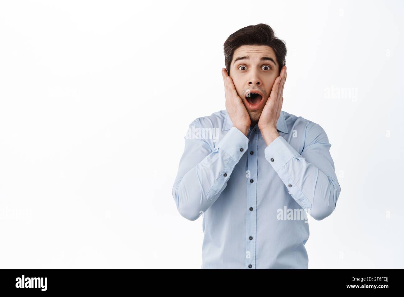 Shocked and startled caucasian man gasping, holding hands on cheeks and ...