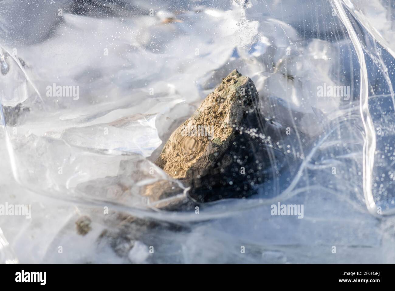 A piece of rock is frozen under the transparent ice. Closeup background ...