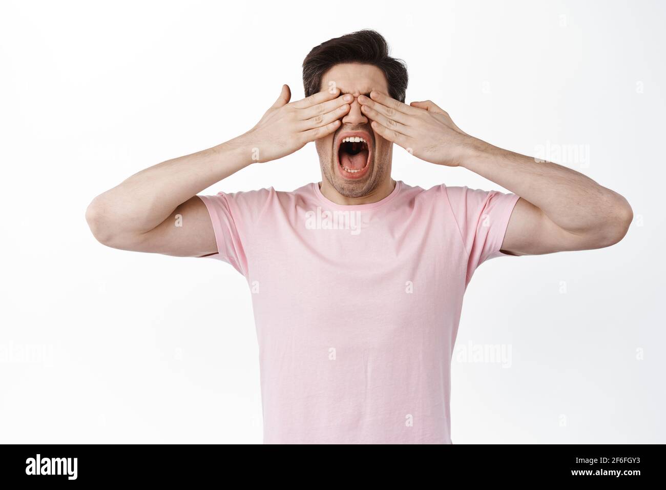 Brunette man covers his eyes with hands and shouting, screaming being ...