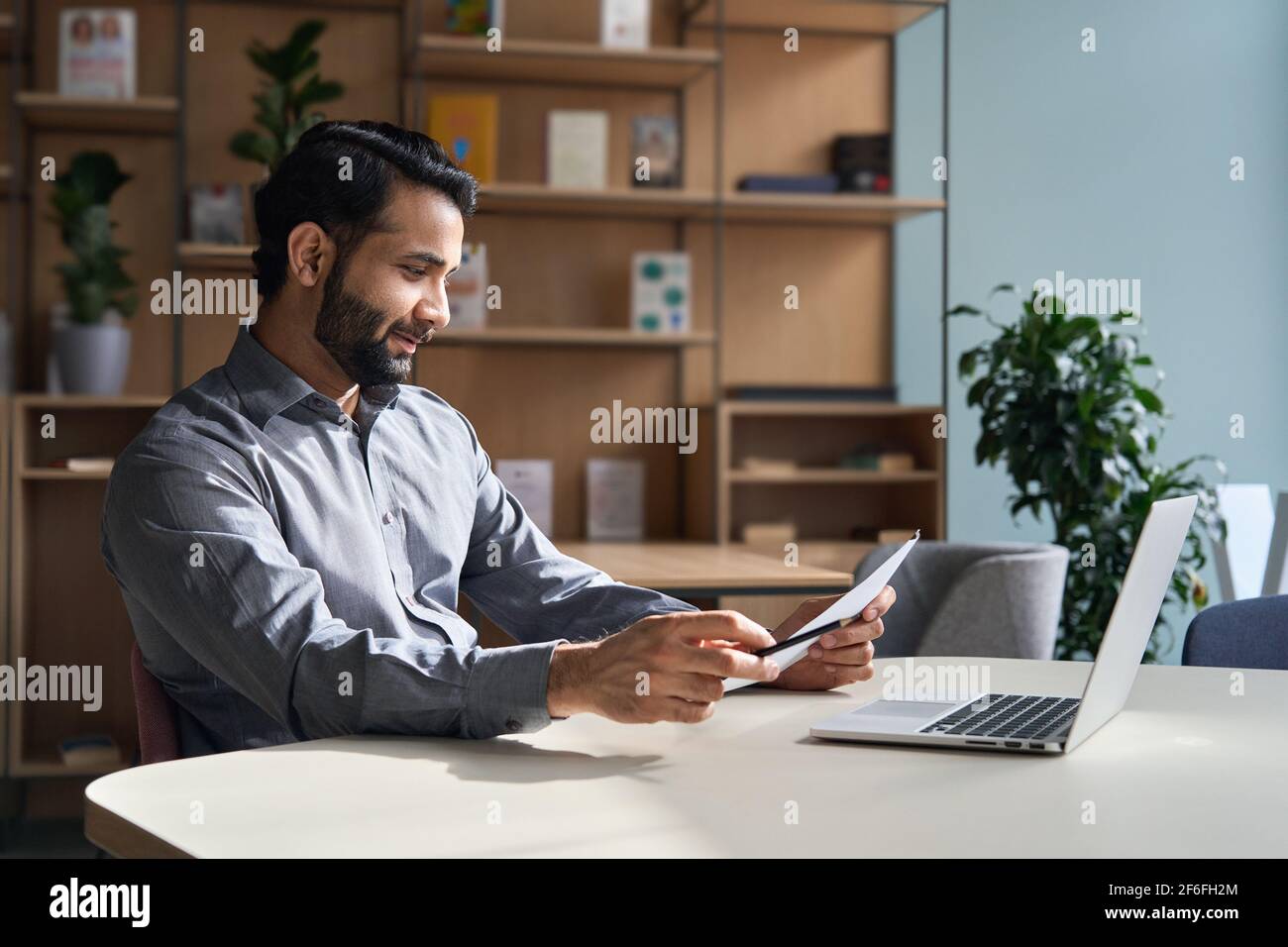 Smiling indian business man working on laptop checking document at home ...