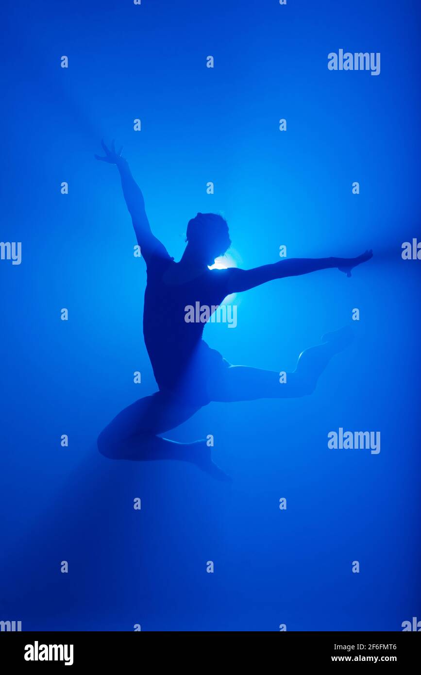 Ballerina in black bodysuit dancing with magic blue light and smoke ...