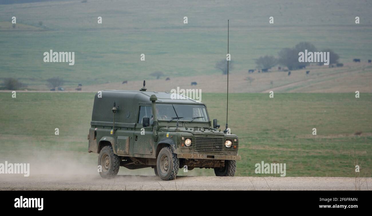 a British Army Land Rover Defender driving along a dusty stone track ...