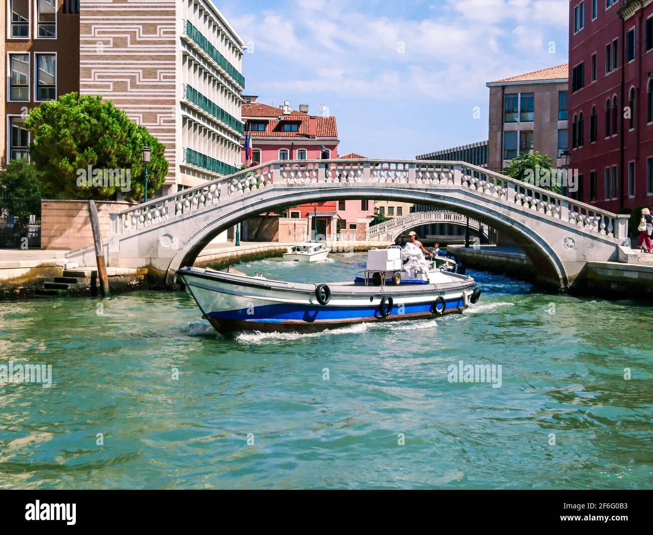 A boat delivery going under white marble bridge on canal in Venice ...