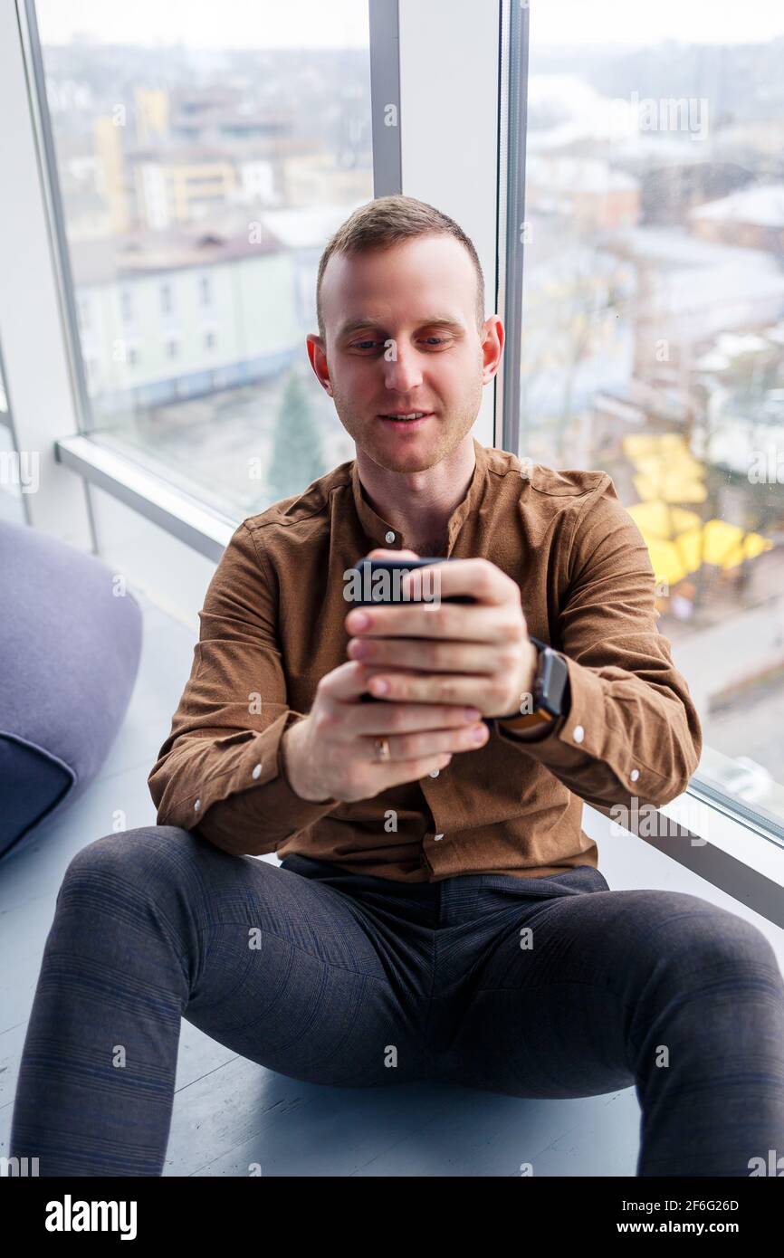 Handsome young male manager is sitting on the floor with the phone near ...