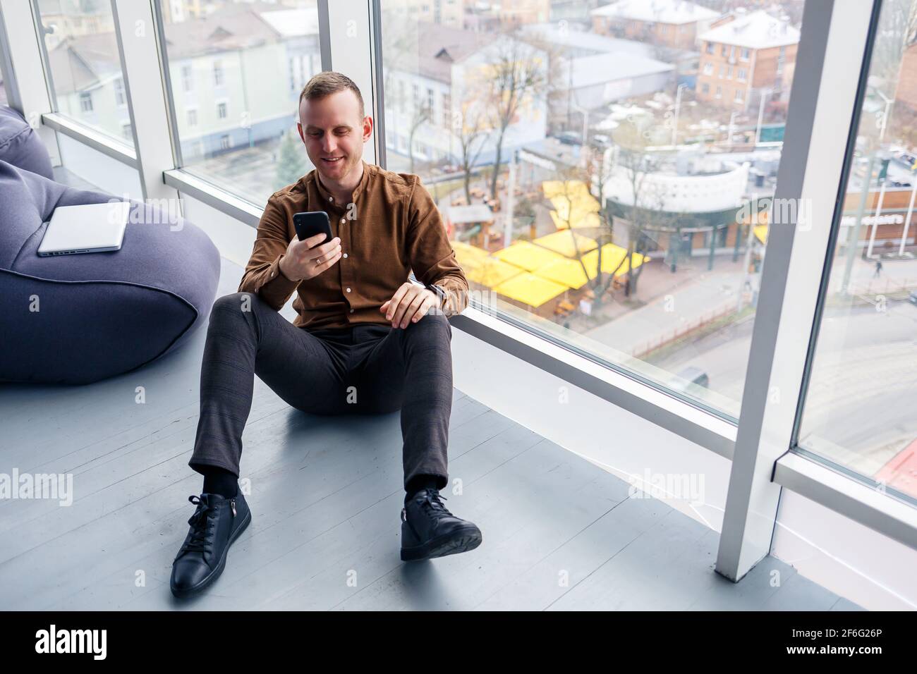 Handsome young male manager is sitting on the floor with the phone near ...