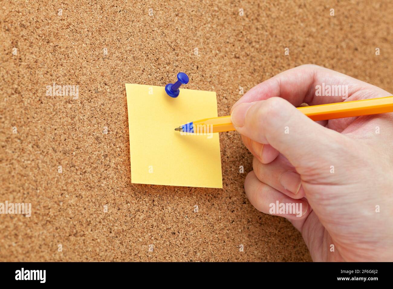 A man writing on a paper note with a ballpoint pen that is pinned on a ...