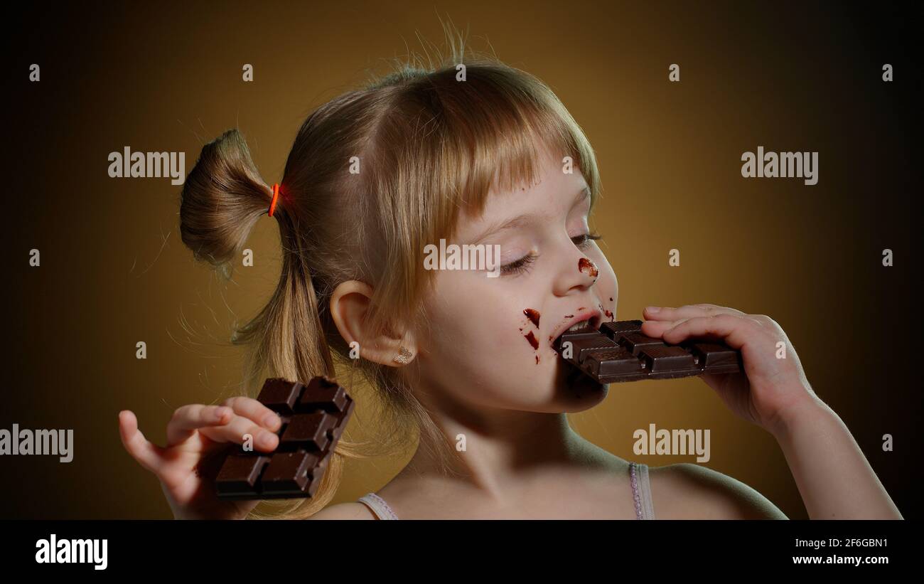 Happy smiling little child girl kid eating milk chocolate bar dessert ...