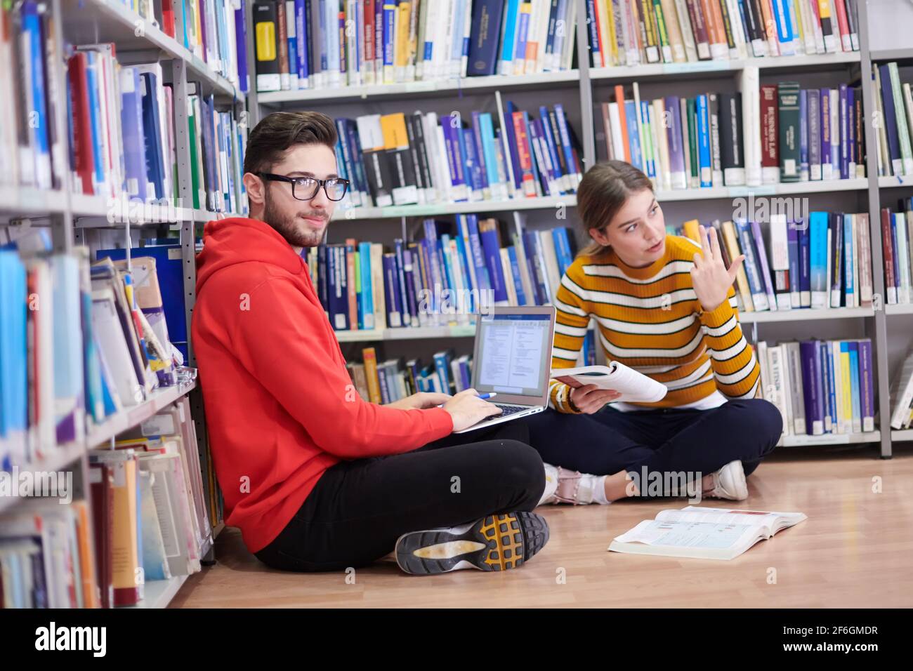 two young students sit in the school library and use a laptop to take ...