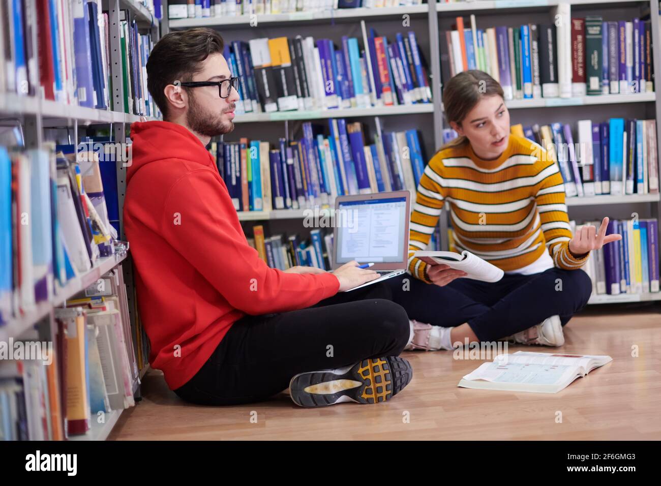 two young students sit in the school library and use a laptop to take ...